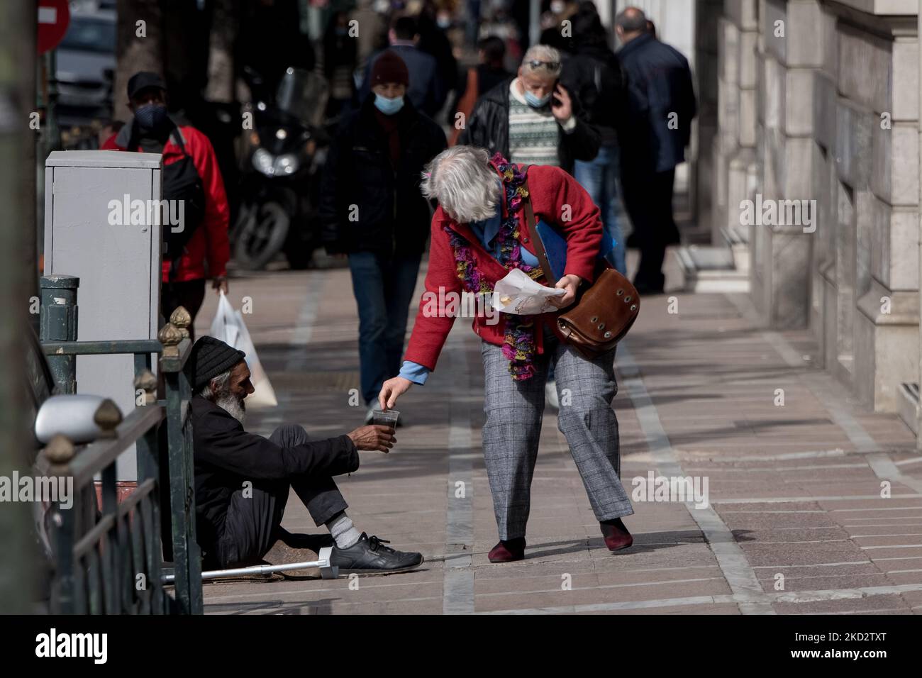 A woman is giving money to a homeless in the center of Athens, Greece ...