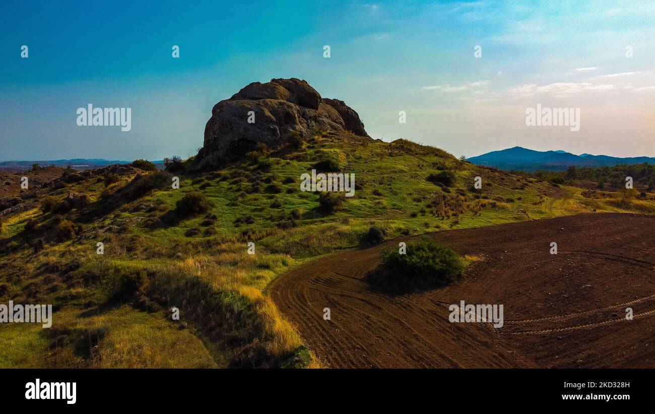 A scenic shot of a boulder on a hill in the middle of a field under the ...