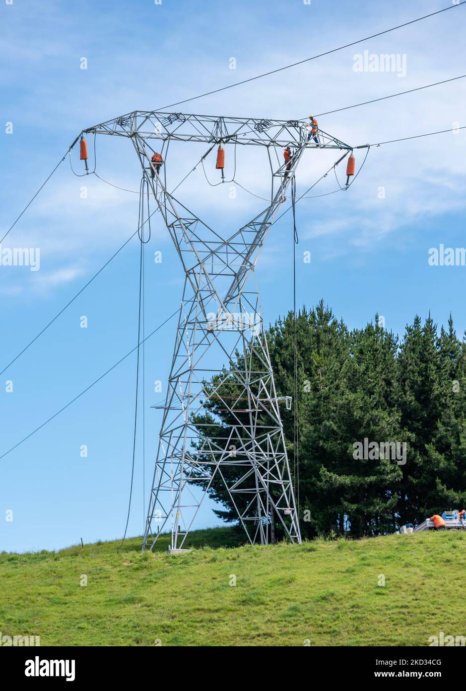 Men working atop an electricity transmission tower maintaining the syst ...