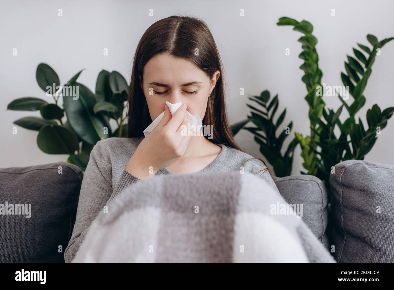 Sick young caucasian woman sitting on grey sofa in living room freezing ...