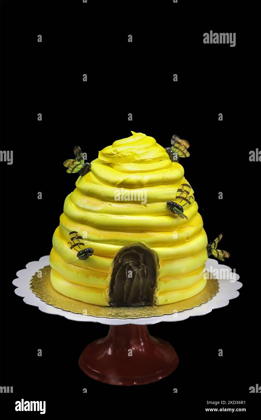 Cute bee hive iced bakery cake on pedestal dish isolated on black with ...