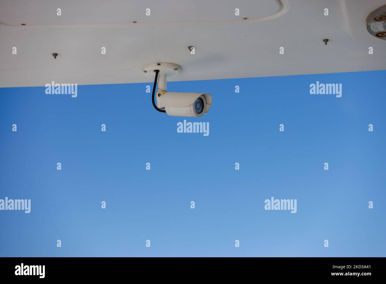 A closeup of a generic security camera mounted overhead with blue sky ...