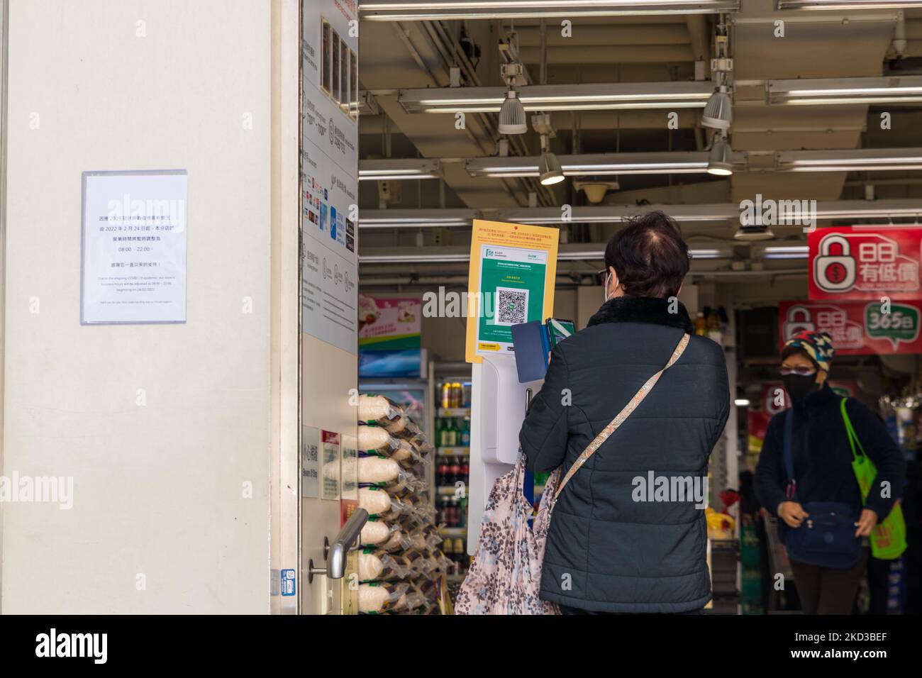 A woman scans the Leave Home Safe QR code before entering a supermarket ...
