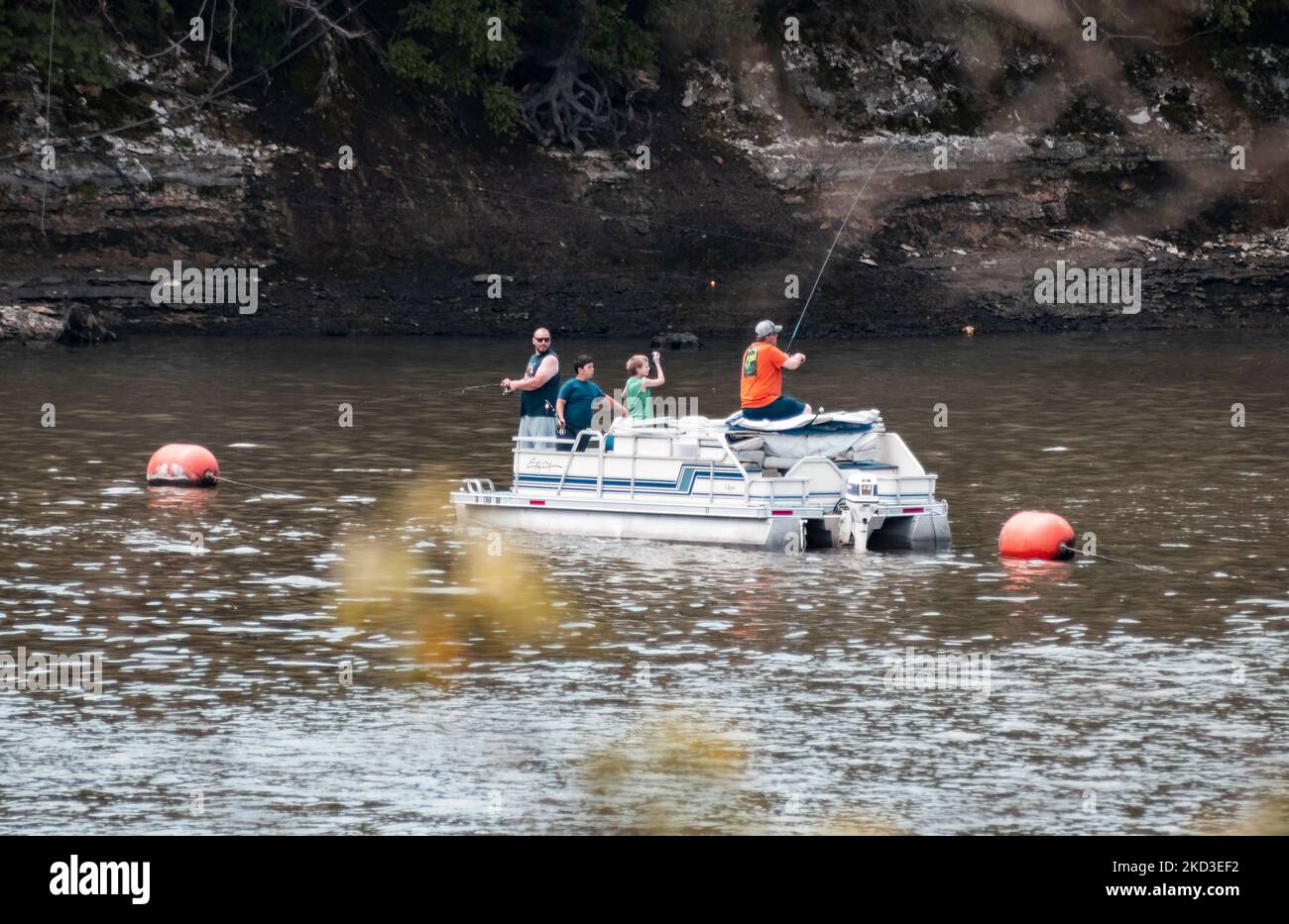 Fathers and sons out in river on pontoon boat fishing with rock cliffs ...