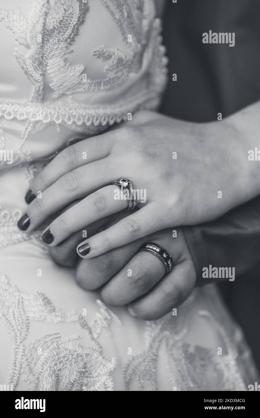 A vertical grayscale closeup of a couple's wedding rings captured on ...