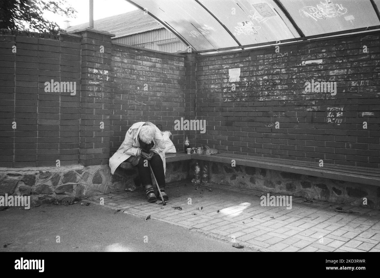 A grayscale shot of a homeless old person sitting on a bench alone ...
