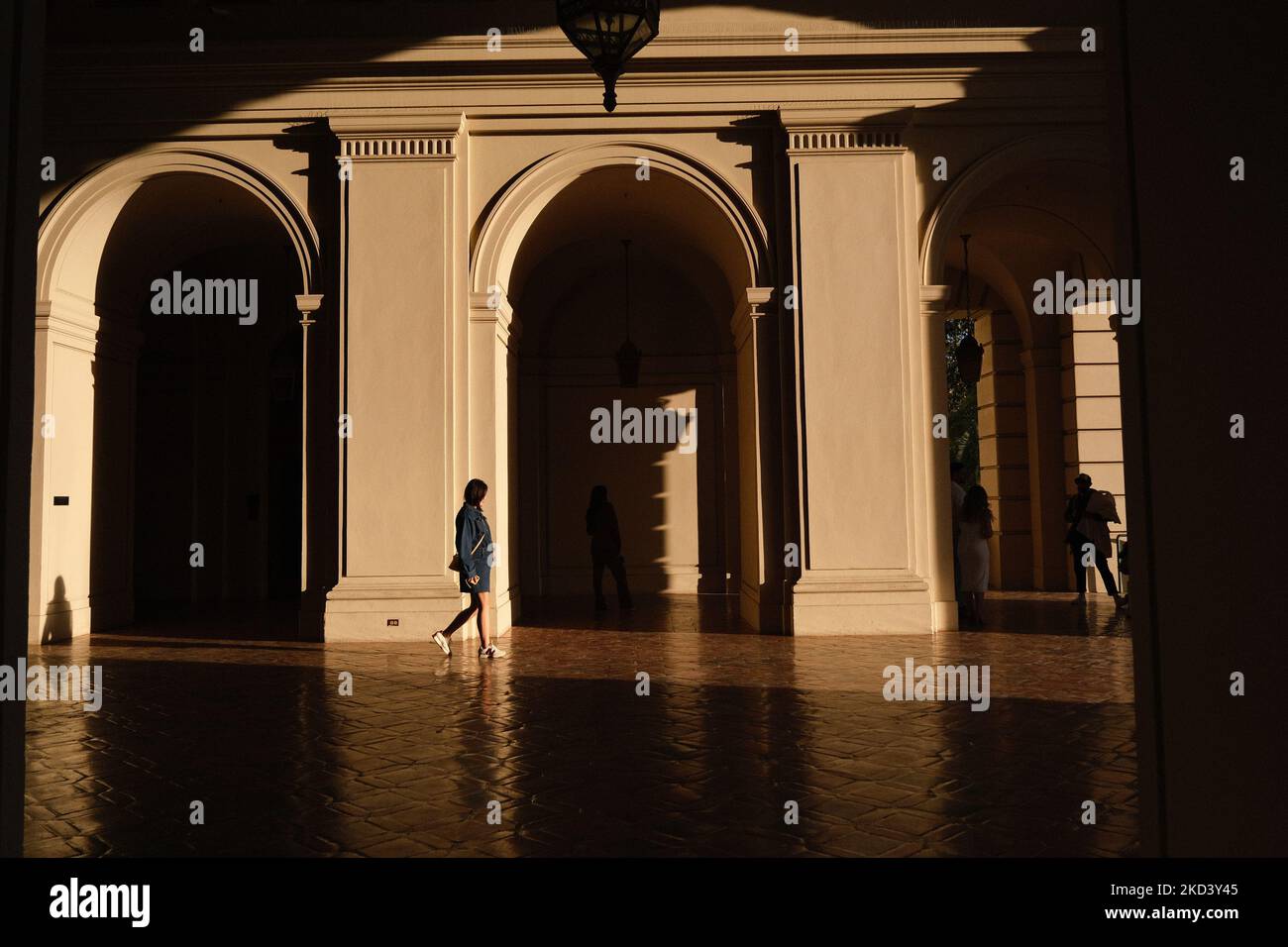 A girl walking through a building with arches, towards the sunlight ...