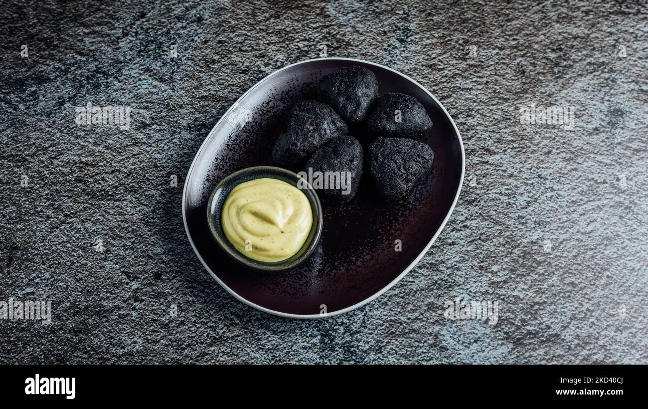A top view of black burned ash potatoes or bread with a mustard sauce ...
