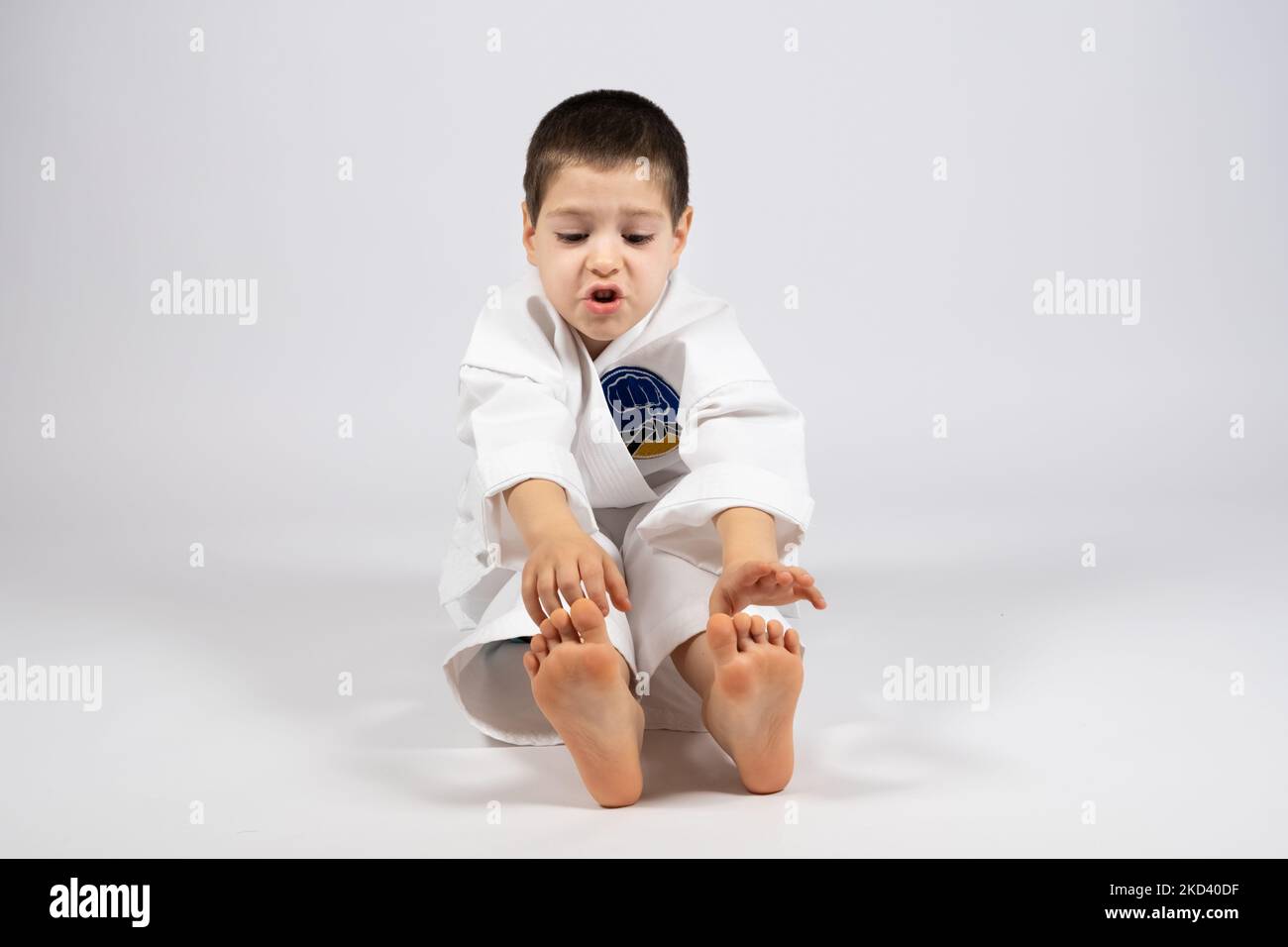 A little boy in a kimono doing karate, stretches his hands to the tips ...