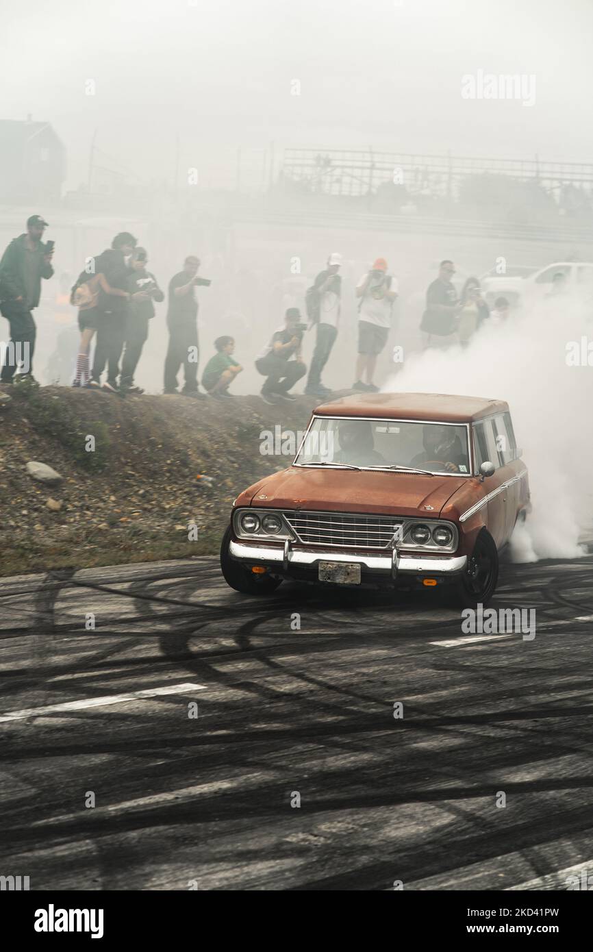 A vertical shot of an old red car doing a burnout on a track in the fog ...