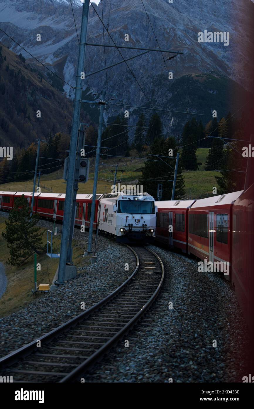 A vertical shot of a red rhb train driving in curve with high mountains ...