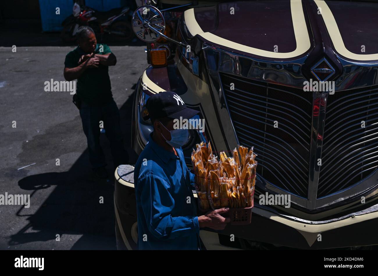 A street vendor passes by a parked Chicken bus at the bus terminal in ...