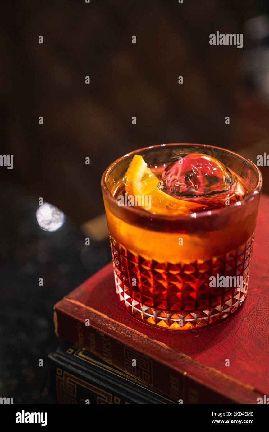 A vertical closeup of an alcoholic drink with round ice and lemon slice ...