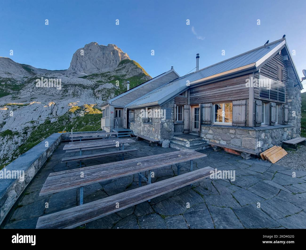 A mountain hut, with solar panels, and benches in front of it, located ...