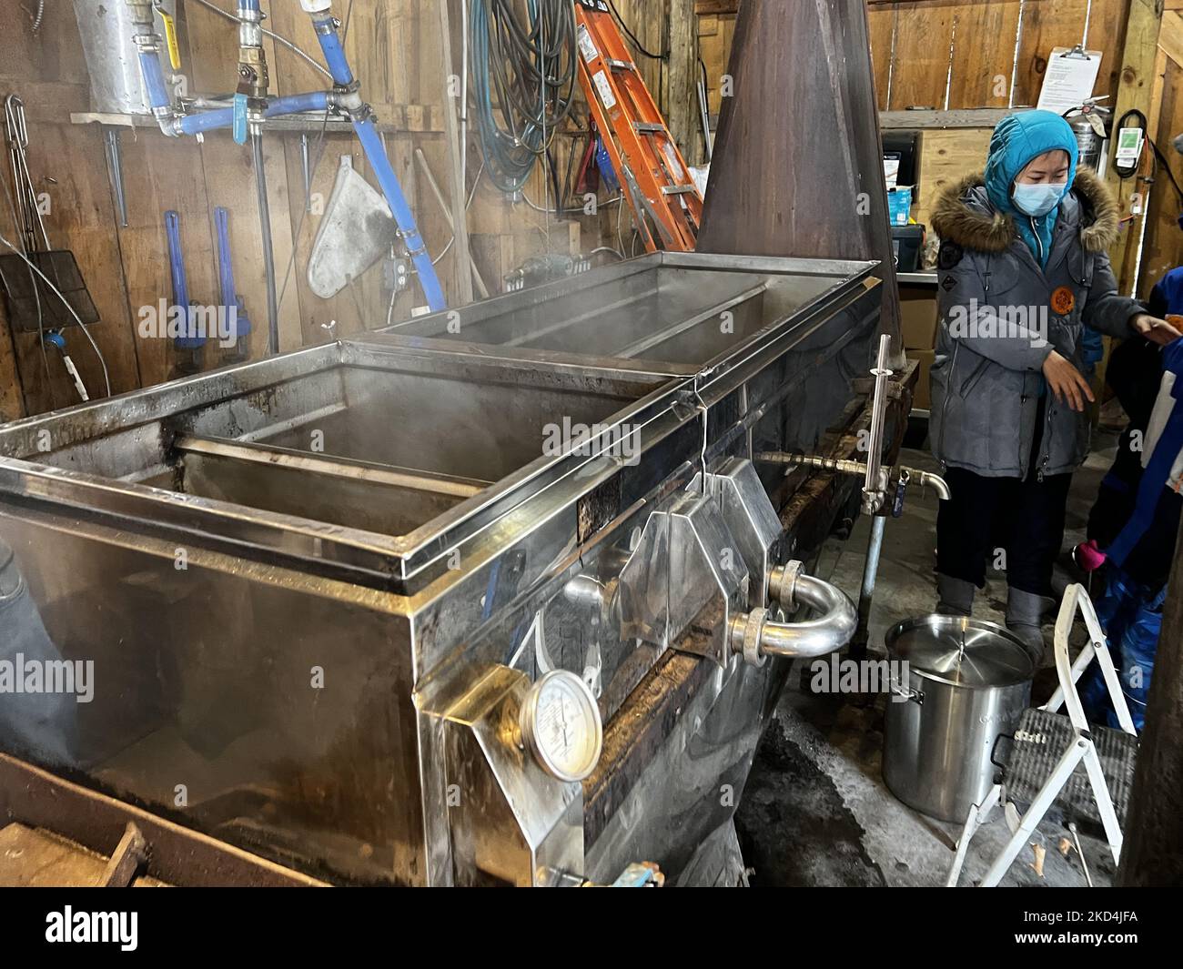 People visiting a maple syrup farm look at the evaporator machine ...