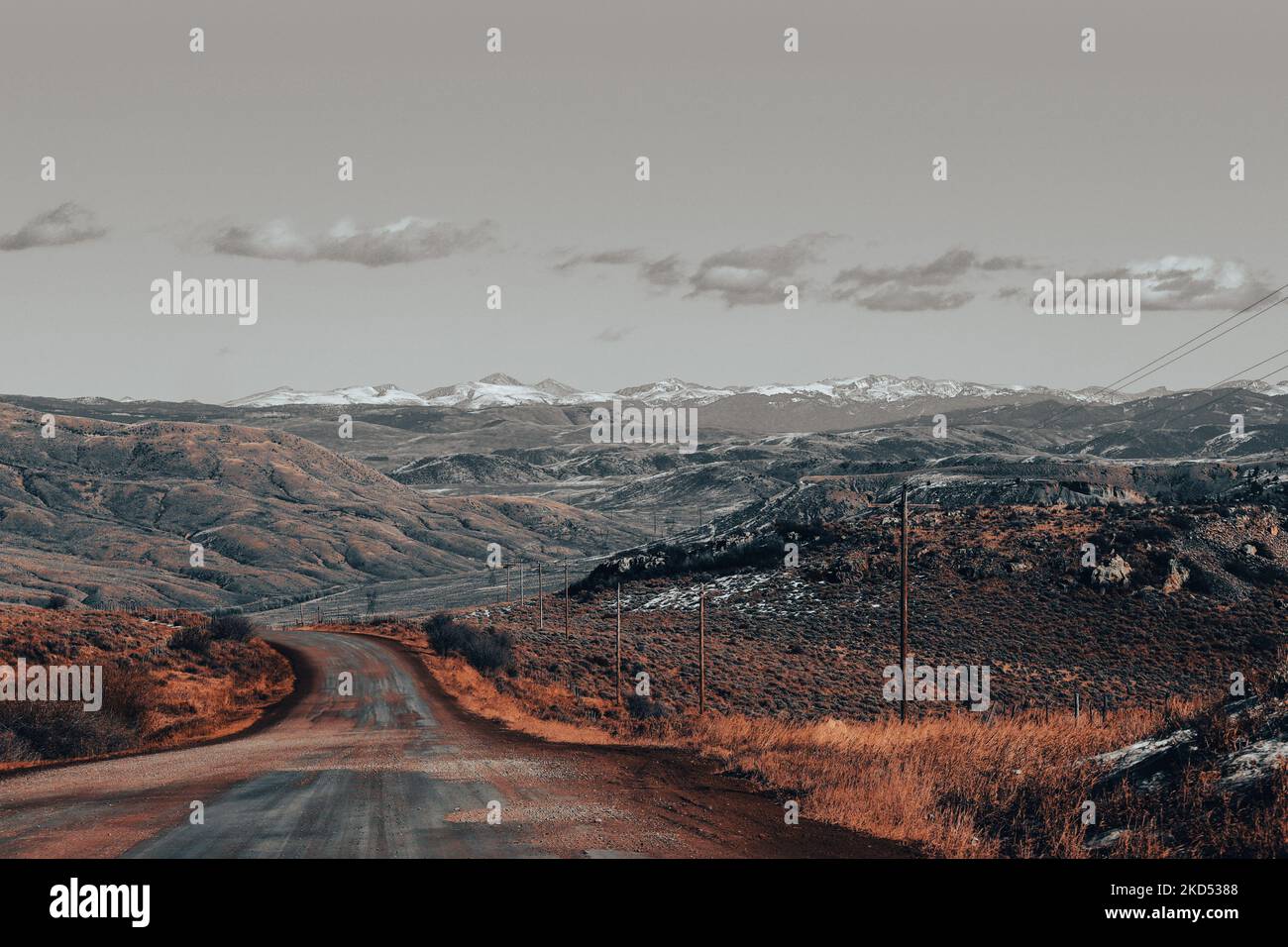 An asphalt desert road going through rocky hills with snow peaked ...