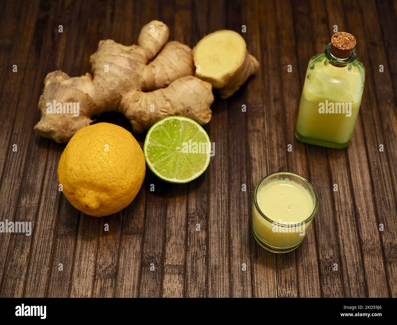A closeup of ginger, lemon, limes and a smoothie on a wooden table ...