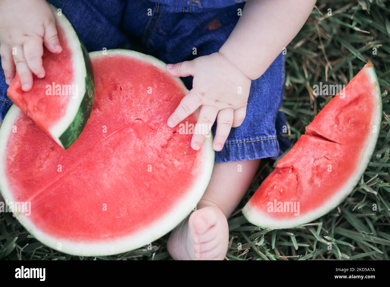 A top view of halved watermelon and slices on sitting baby's feet Stock ...