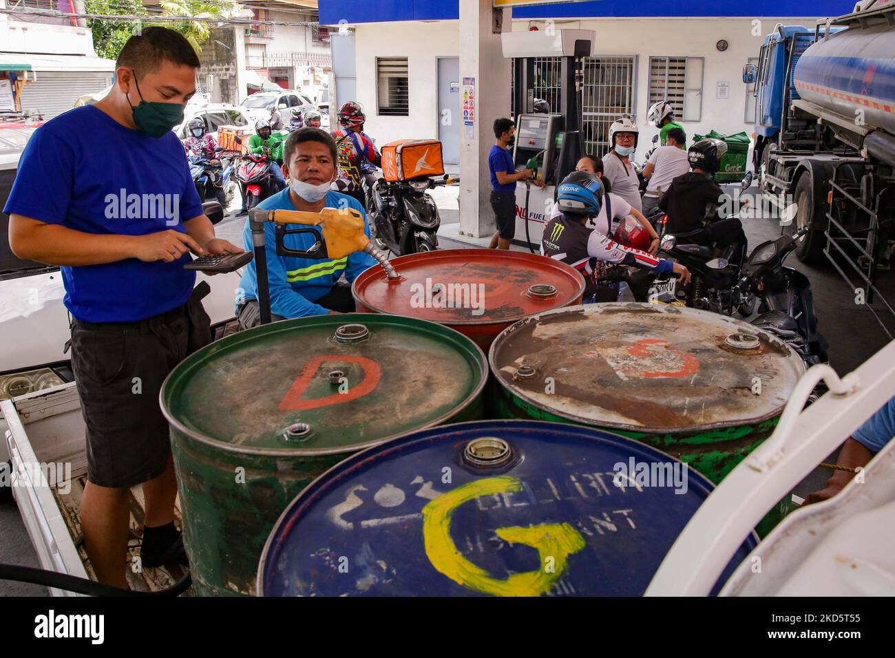 A worker pumps fuel into multiple barrels while other motorists line up ...