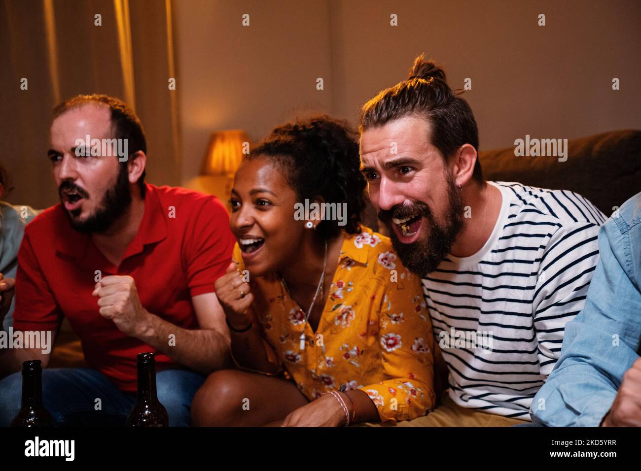Group of three young friends sitting on the couch and watching sports ...