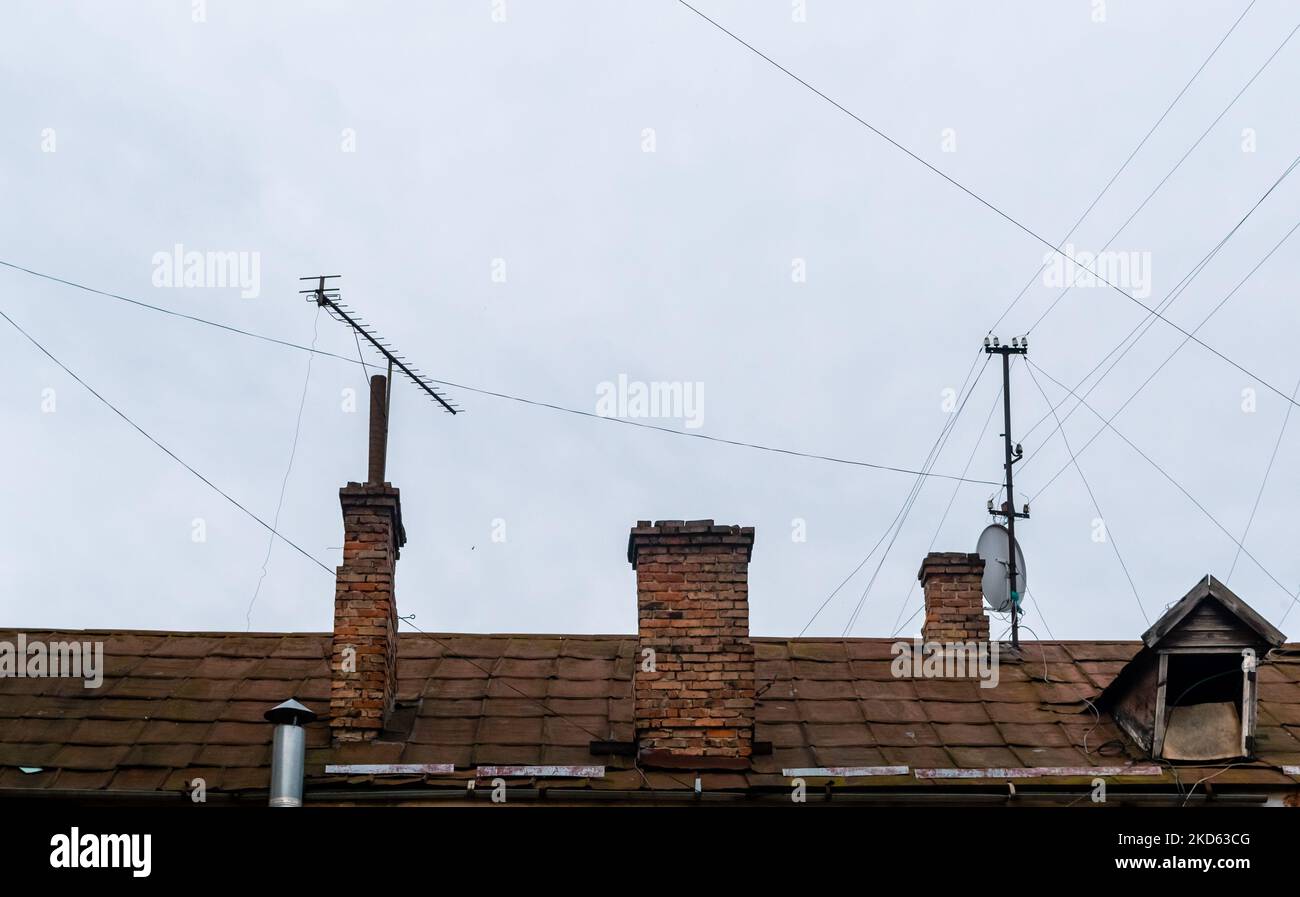 Roof of old house with brick chimneys and electrical wires on gray sky ...