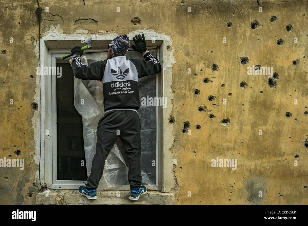 A man repairs the window of his home destroyed by russian artillery ...