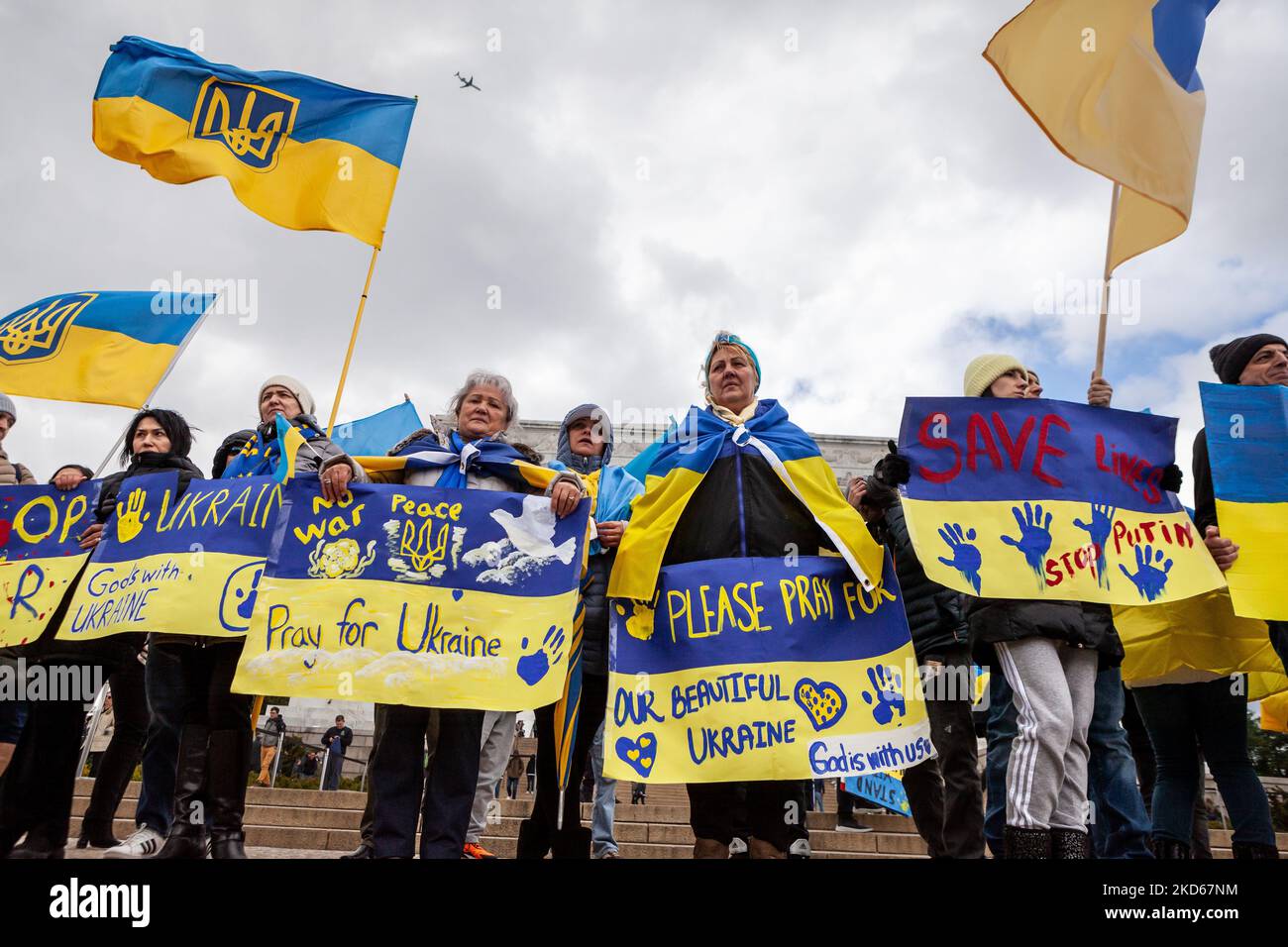 Protesters display flags and signs behind the podium and speakers ...