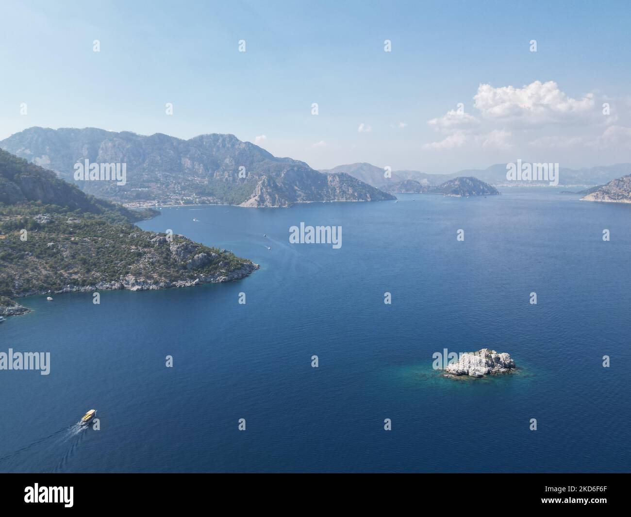 A blue sea with big cliffs and mountains in the background under a blue ...