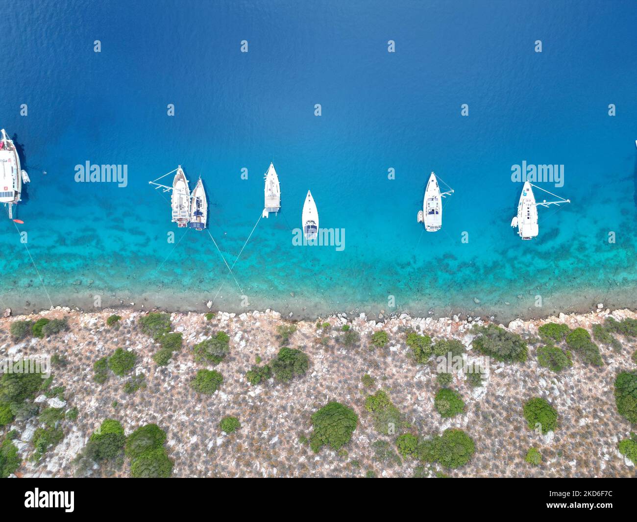 A top view of white boats in a beautiful blue sea docked on the shore ...