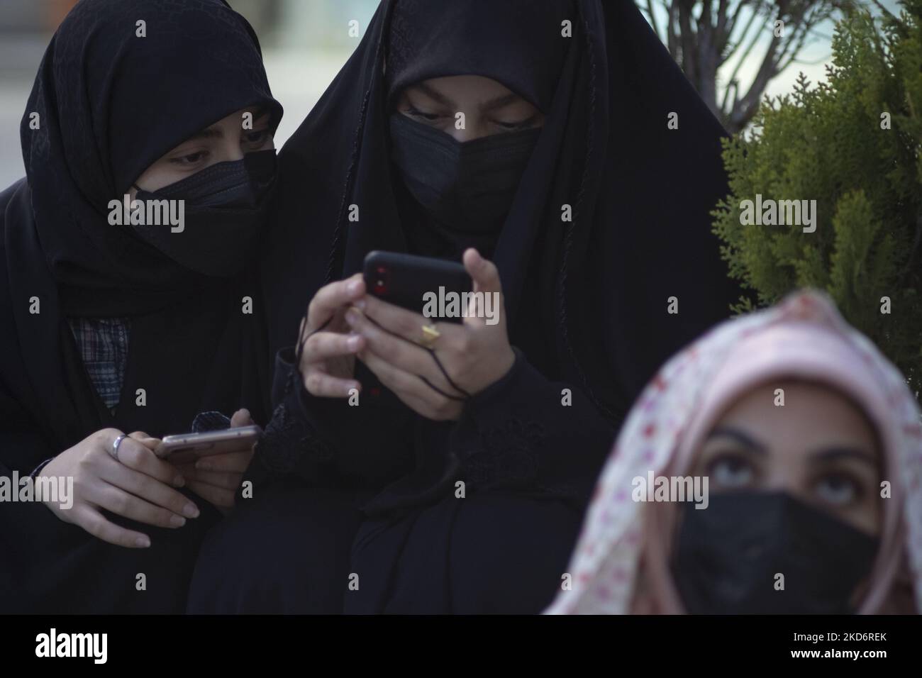 Two veiled women wearing protective face masks use their smartphones in ...