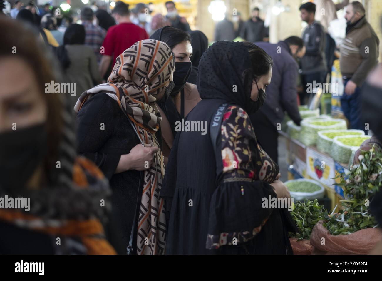 Iranian women wearing protective face masks look at vegetables while ...