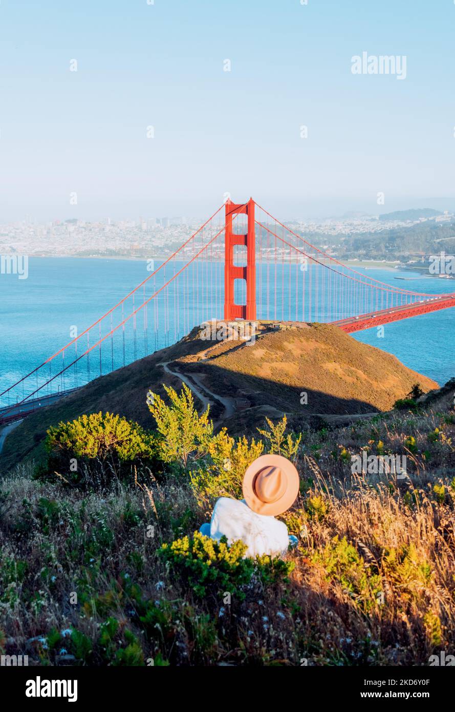 A vertical shot of a tourist with a hat looking at the Golden Gate ...