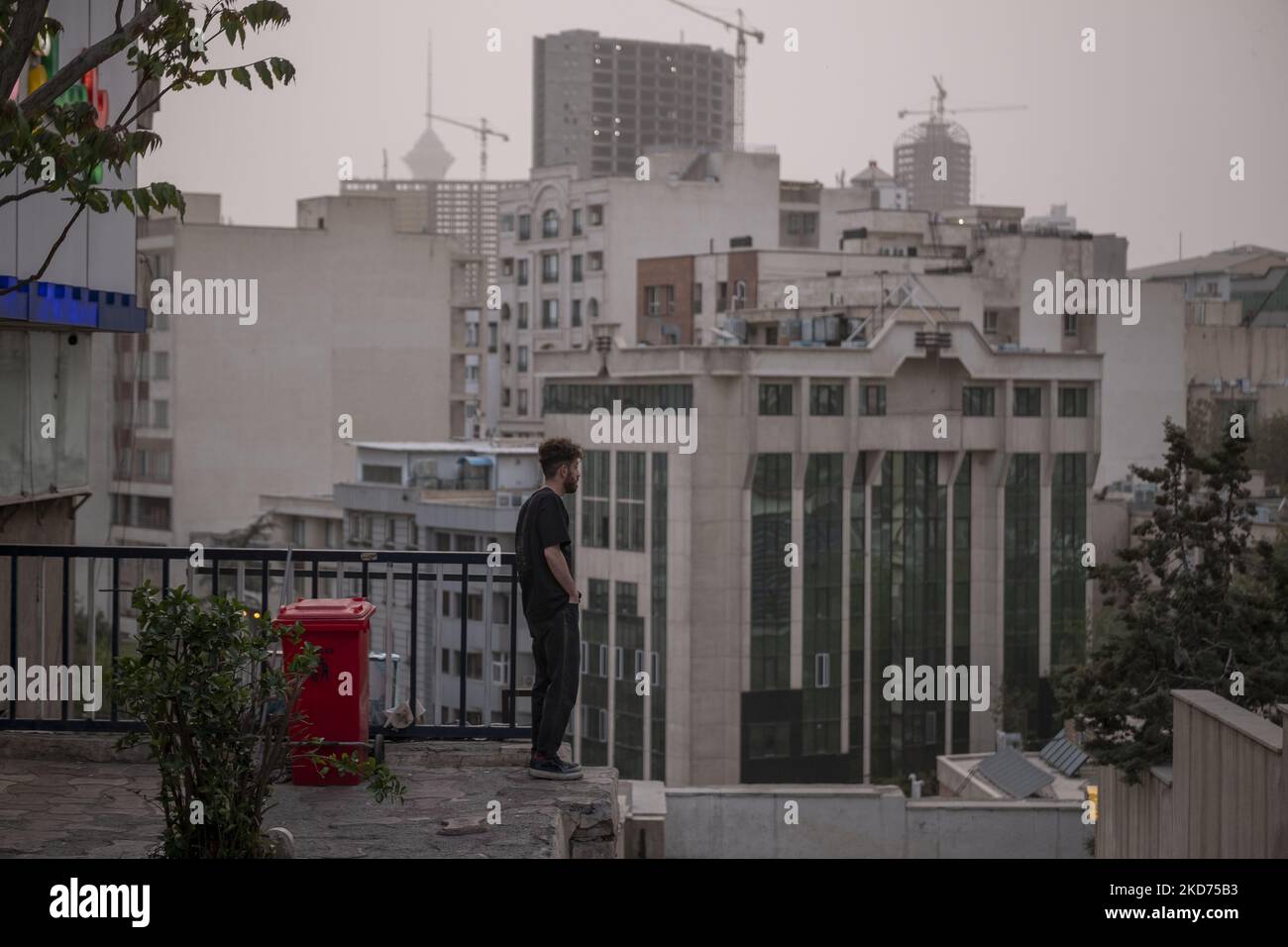 An Iranian man stands on a street-side as a view of downtown Tehran ...
