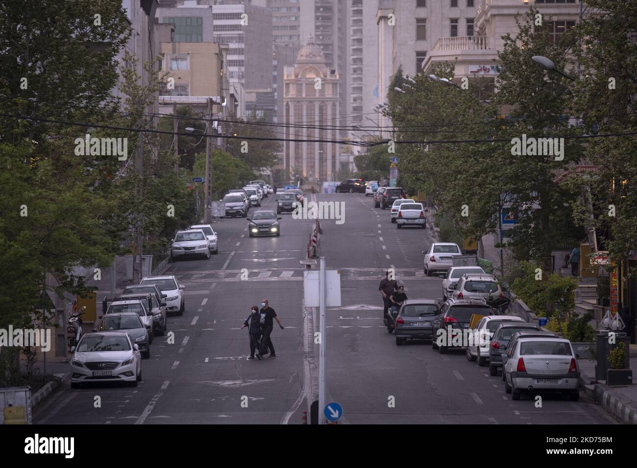 An Iranian couple wearing protective face masks cross a street in ...
