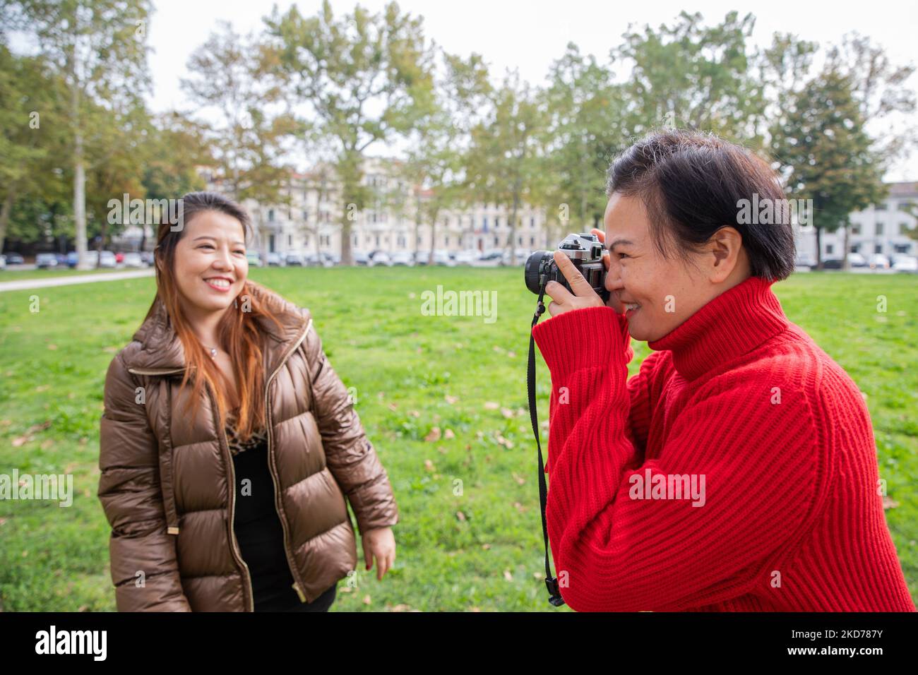 A friend taking photos of her friend with analog camera at the city ...