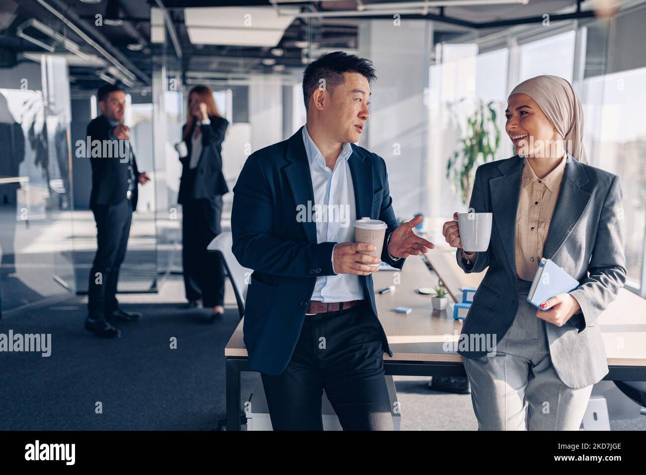 Two happy multiracial colleagues talking and drinking coffee during ...