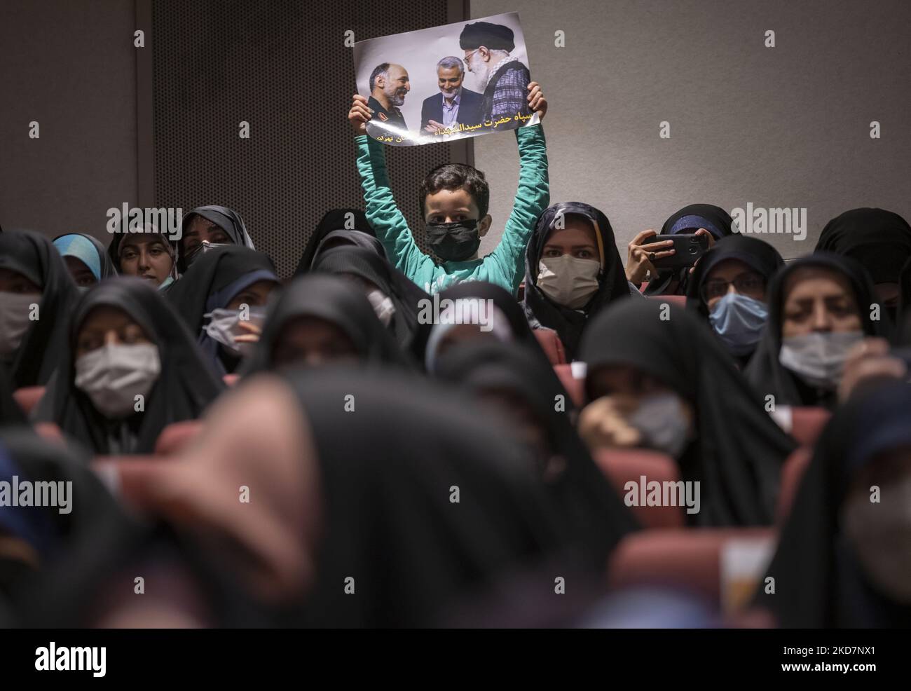 An Iranian young boy wearing a protective face mask holds-up a poster ...