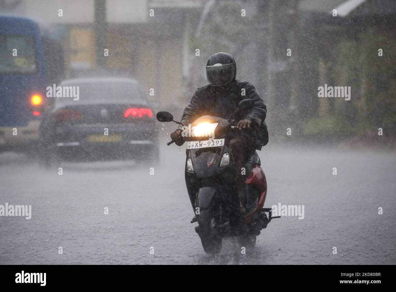 A man rides a motorbike through a road during a heavy rain shower in ...