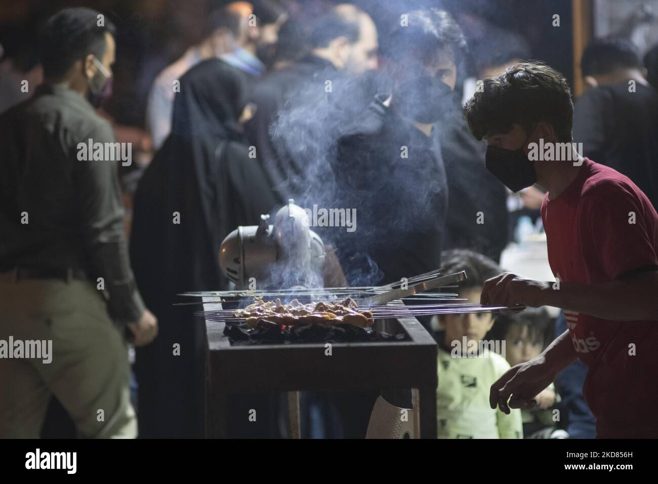 A worker wearing a protective face mask prepares chicken barbecue for ...