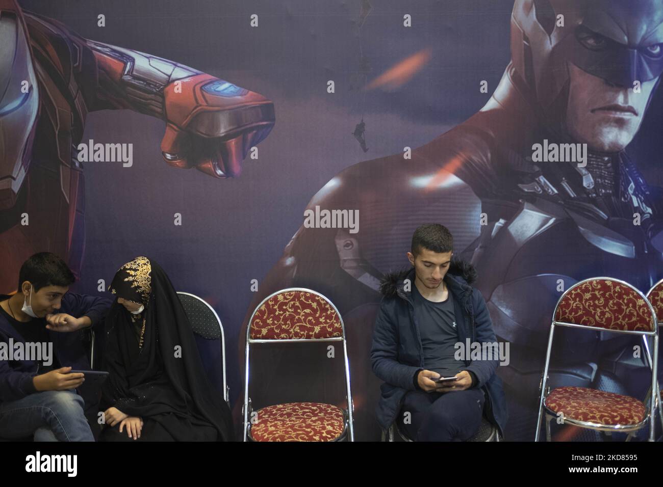 Iranian youths sit under a banner with Images of American superheroes ...