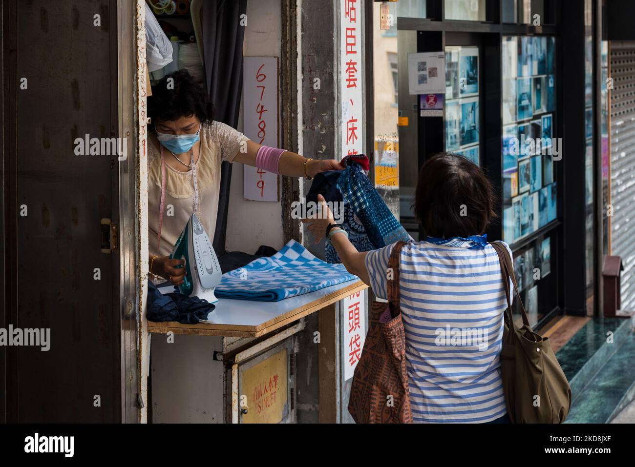 Hong Kong, China, 28 Apr 2022, A store owner hands over an ironed dress ...