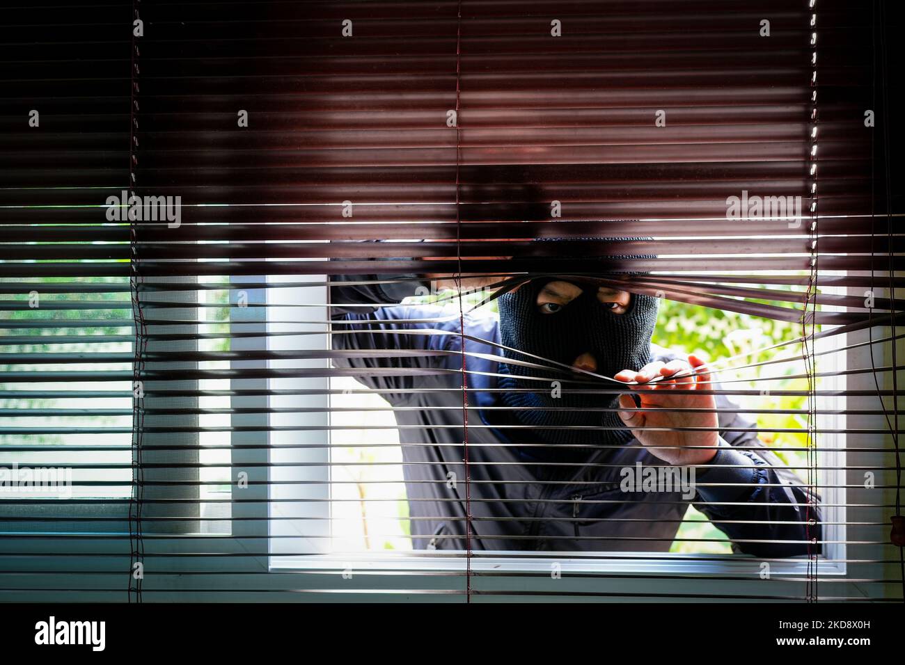 A man wearing a balaclava on his face looking throw the window- a ...