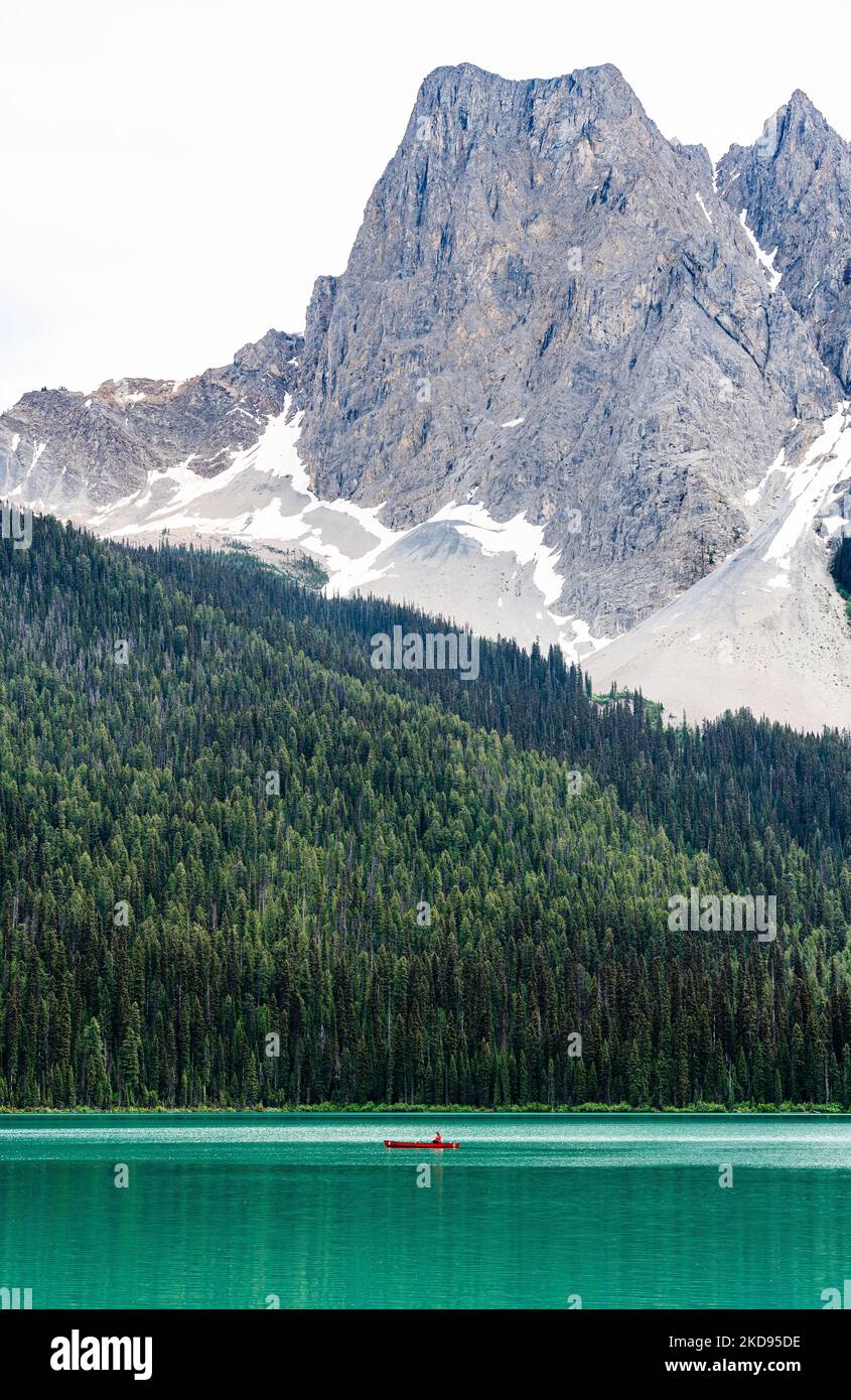 A beautiful scenery of a rocky mountain with trees and a small red boat ...