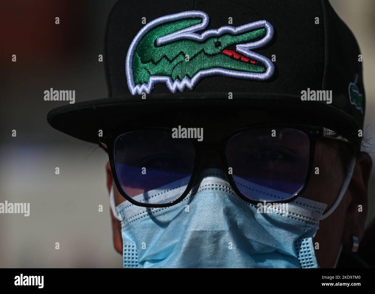 A young man seen wearing a Lacoste hat and a medical face mask. On ...