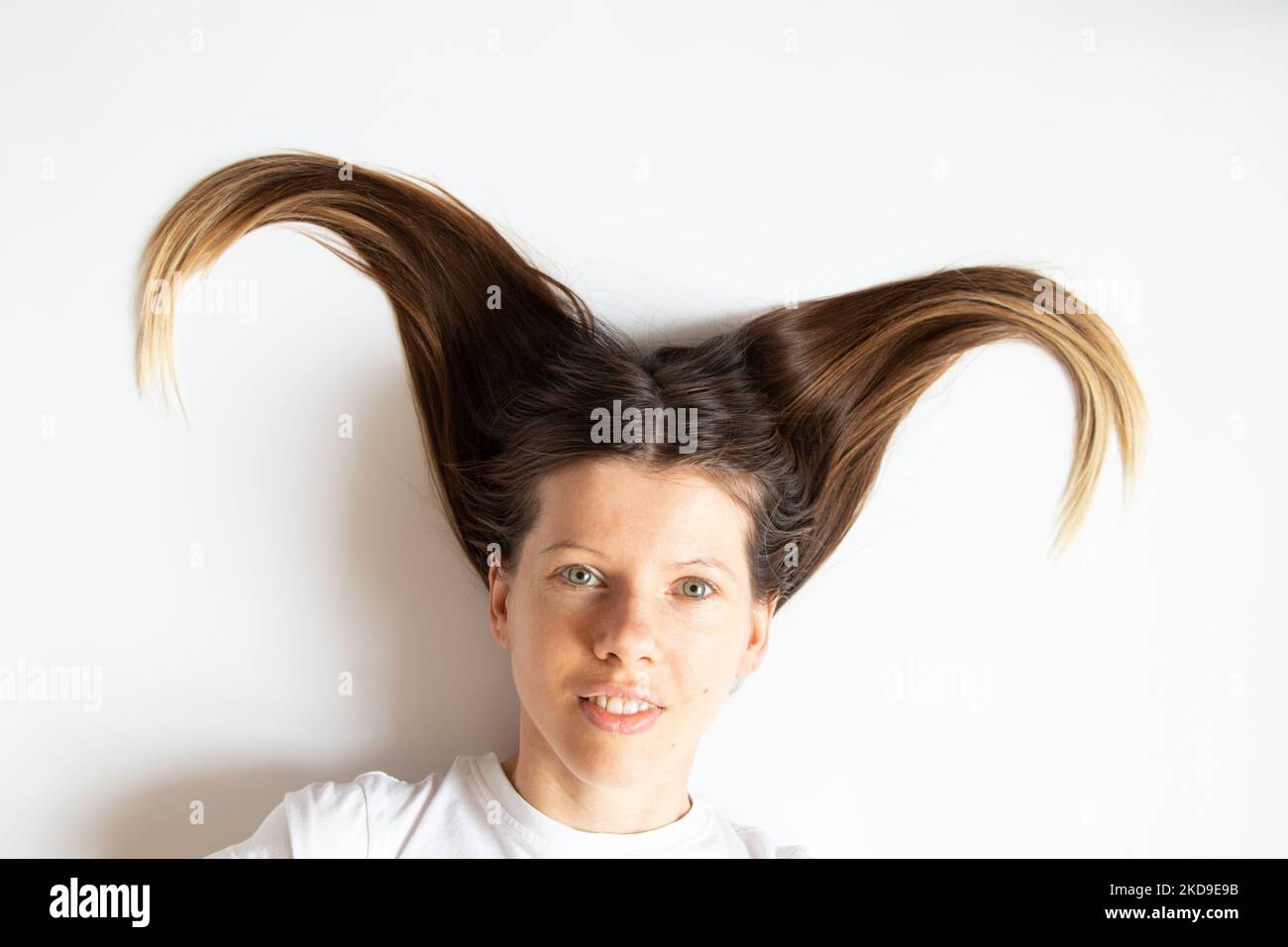 A girl with long hair and a smile lies on a white background, an ...