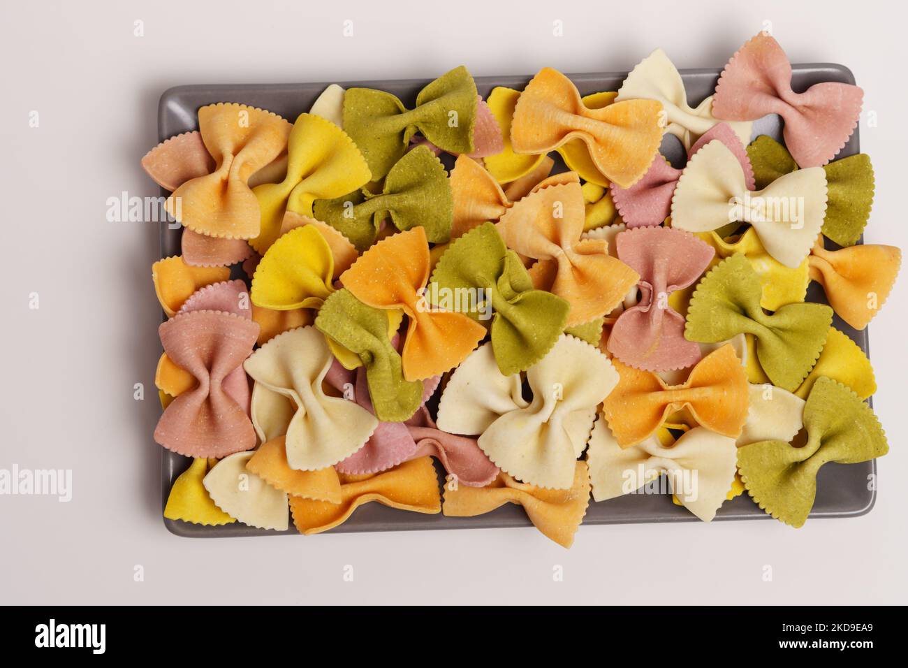 colored raw farfalle pasta on a gray tray isolated on a white ...