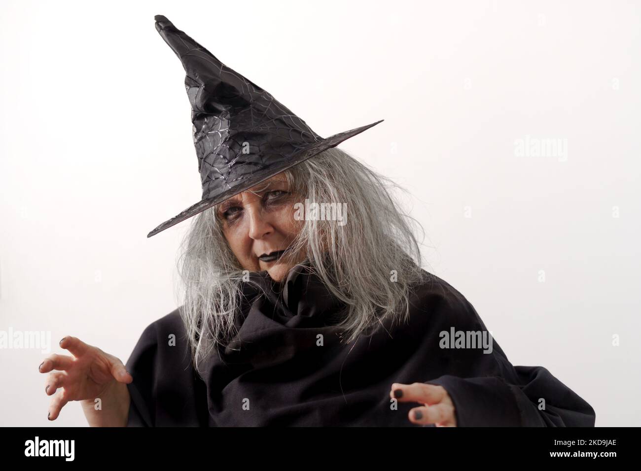 A closeup of a white-haired witch in a black hat and costume on a white ...