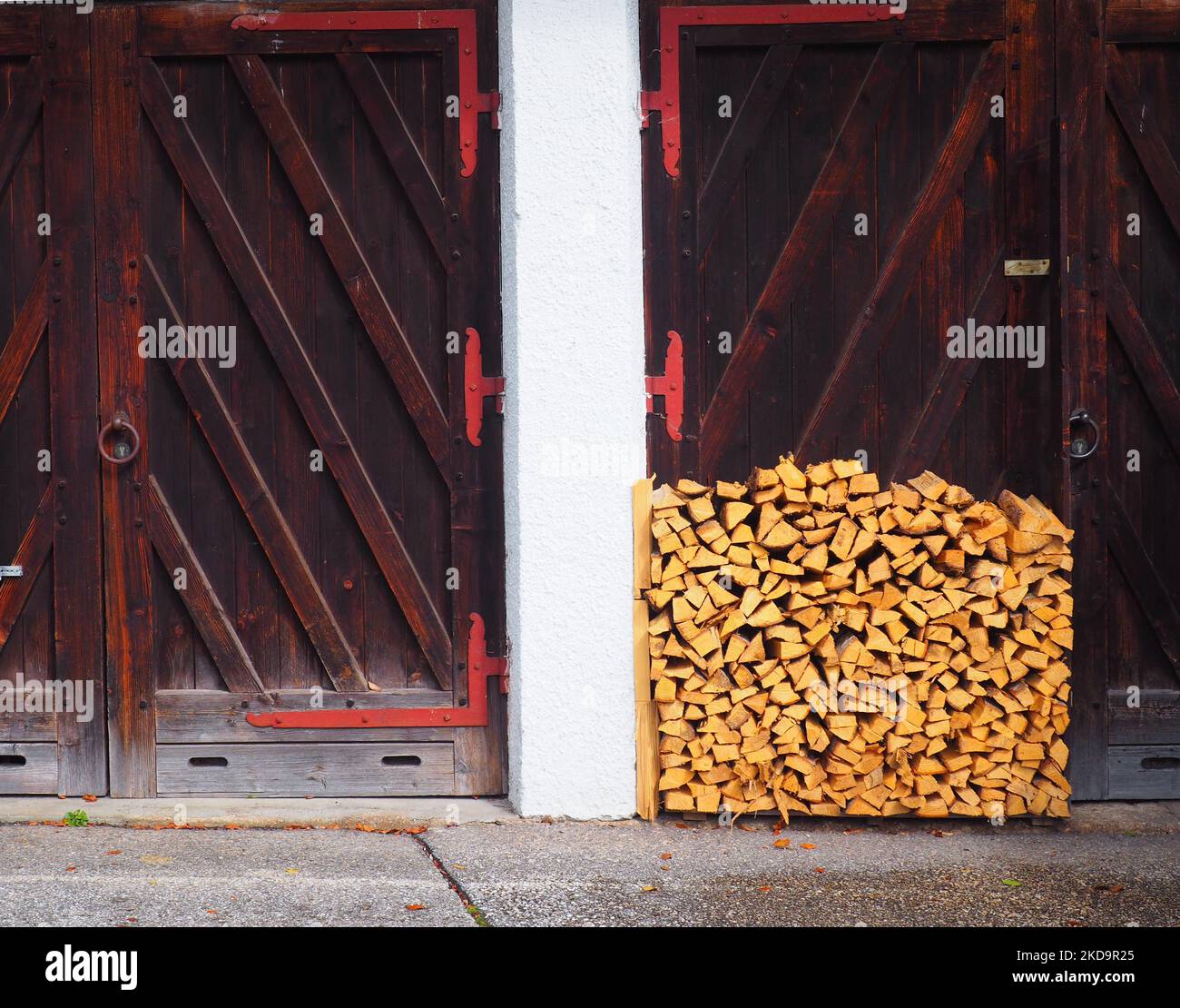 A stack of freshly cut firewood logs on the ground in front of a wooden ...