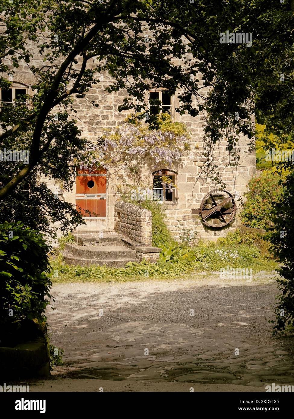 An unpaved street in front of an old stone house with trees on a sunny ...