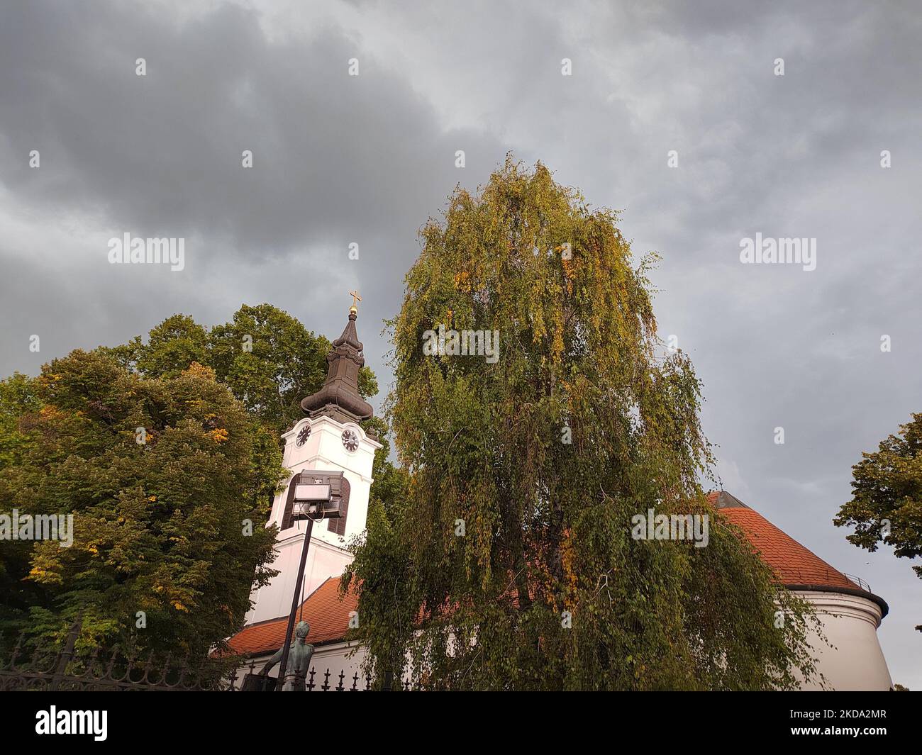 A low angle shot of Catholic church behind green trees on a cloudy day ...